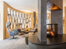 Espaço de descanso com lareira de pedra, assentos de design exclusivo e padrão geométrico na parede.