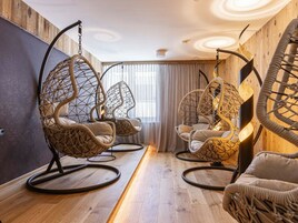 Quarto com cadeiras penduradas, piso de madeira e uma grande janela com cortinas.