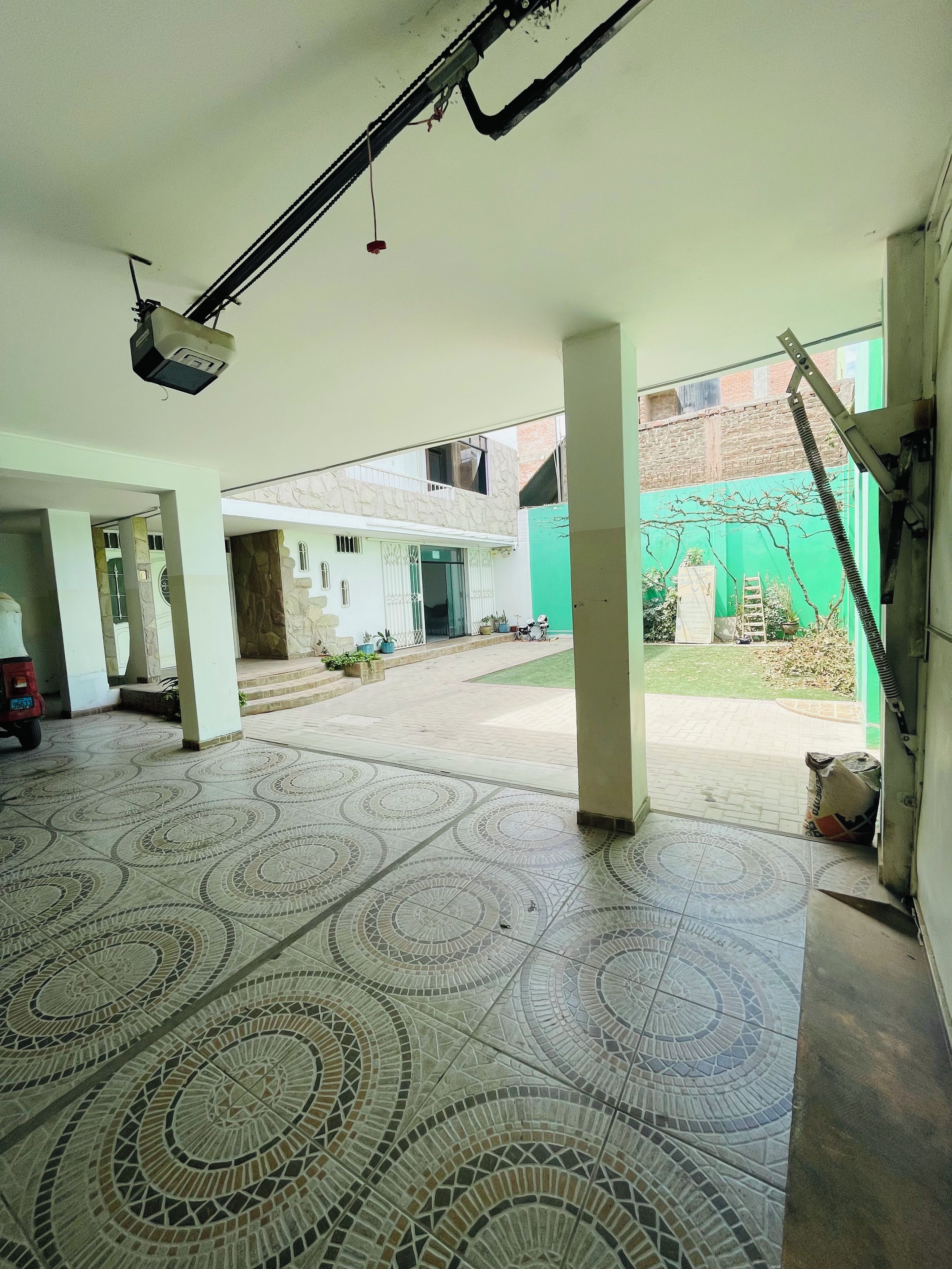 Amplo espaço interno com piso estampado, escada que leva a área externa e parede verde visível através de uma janela.