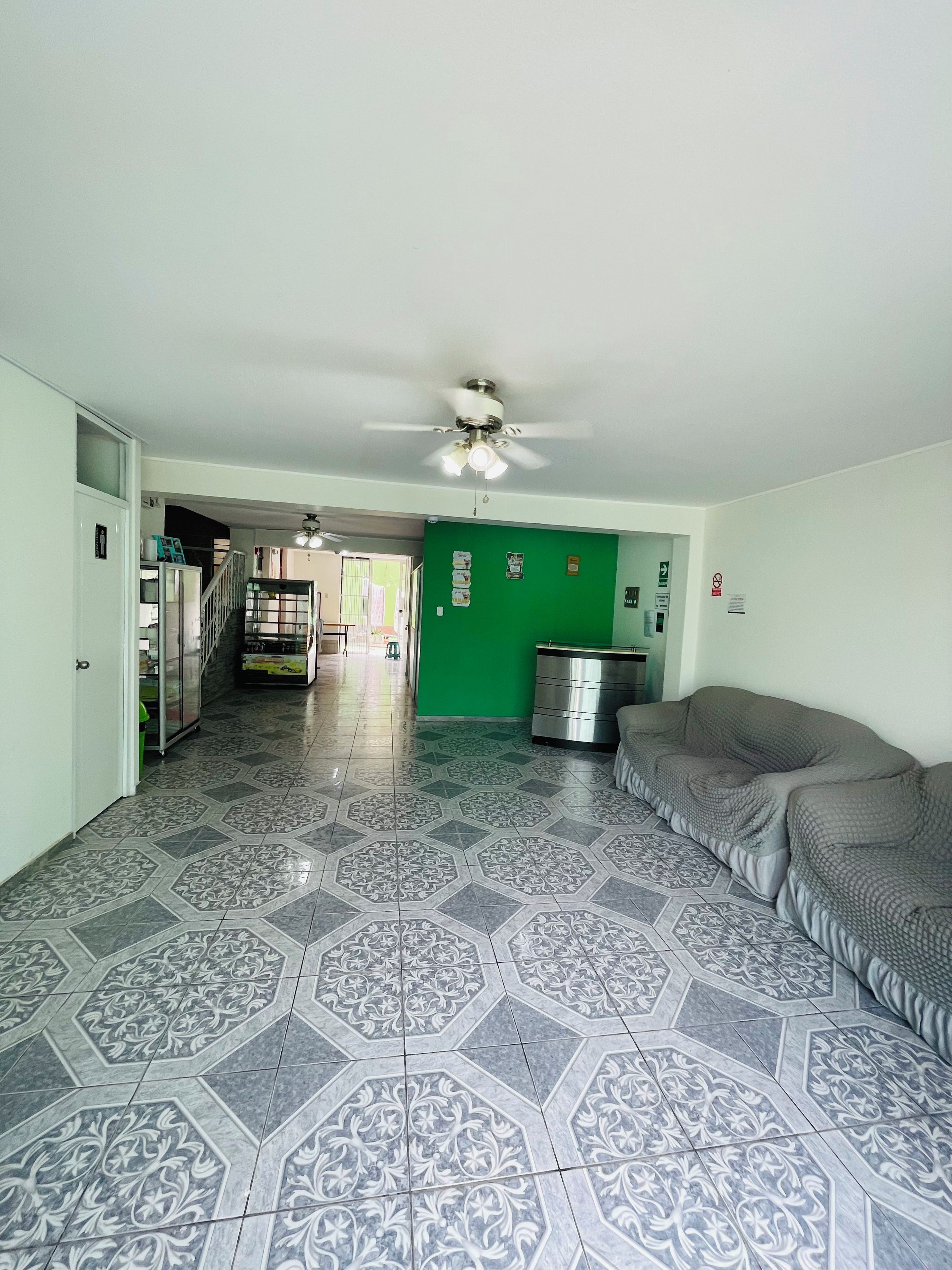 Uma sala de estar espaçosa, com ladrilhos estampados, ventilador de teto e uma parede verde.