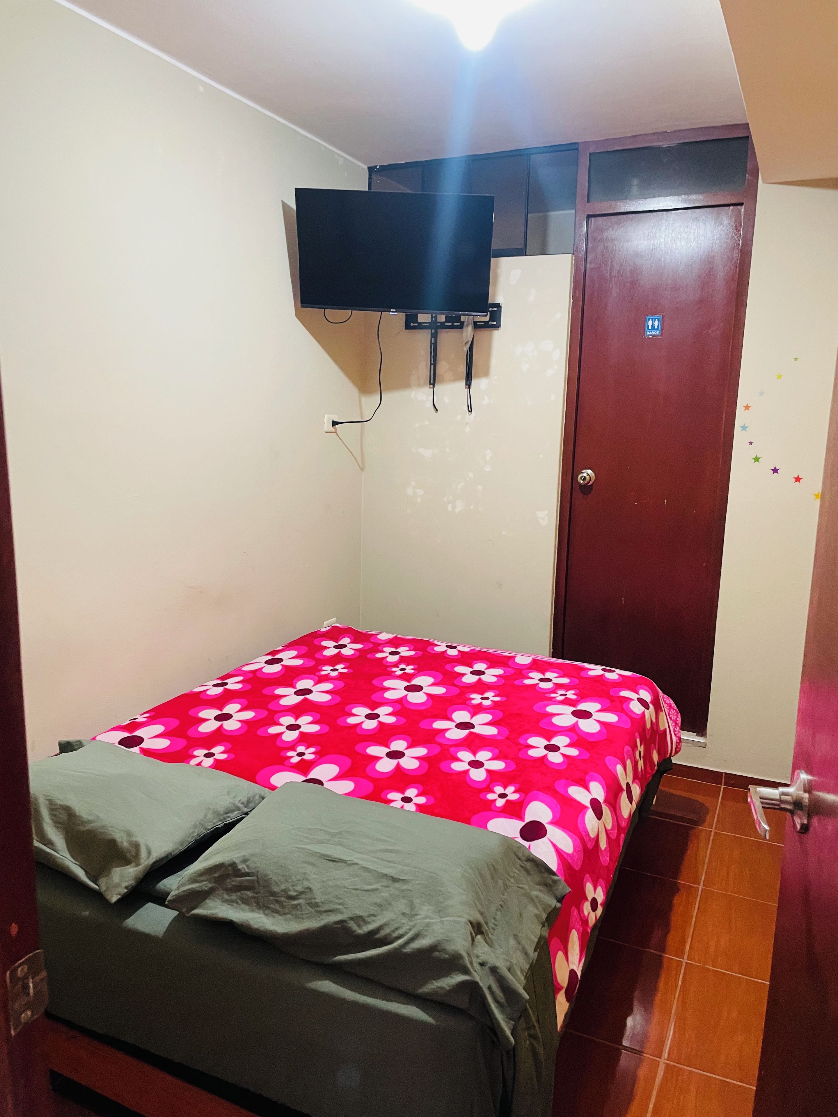 Quarto com cama, televisão fixada na parede e porta com o símbolo de acessibilidade.