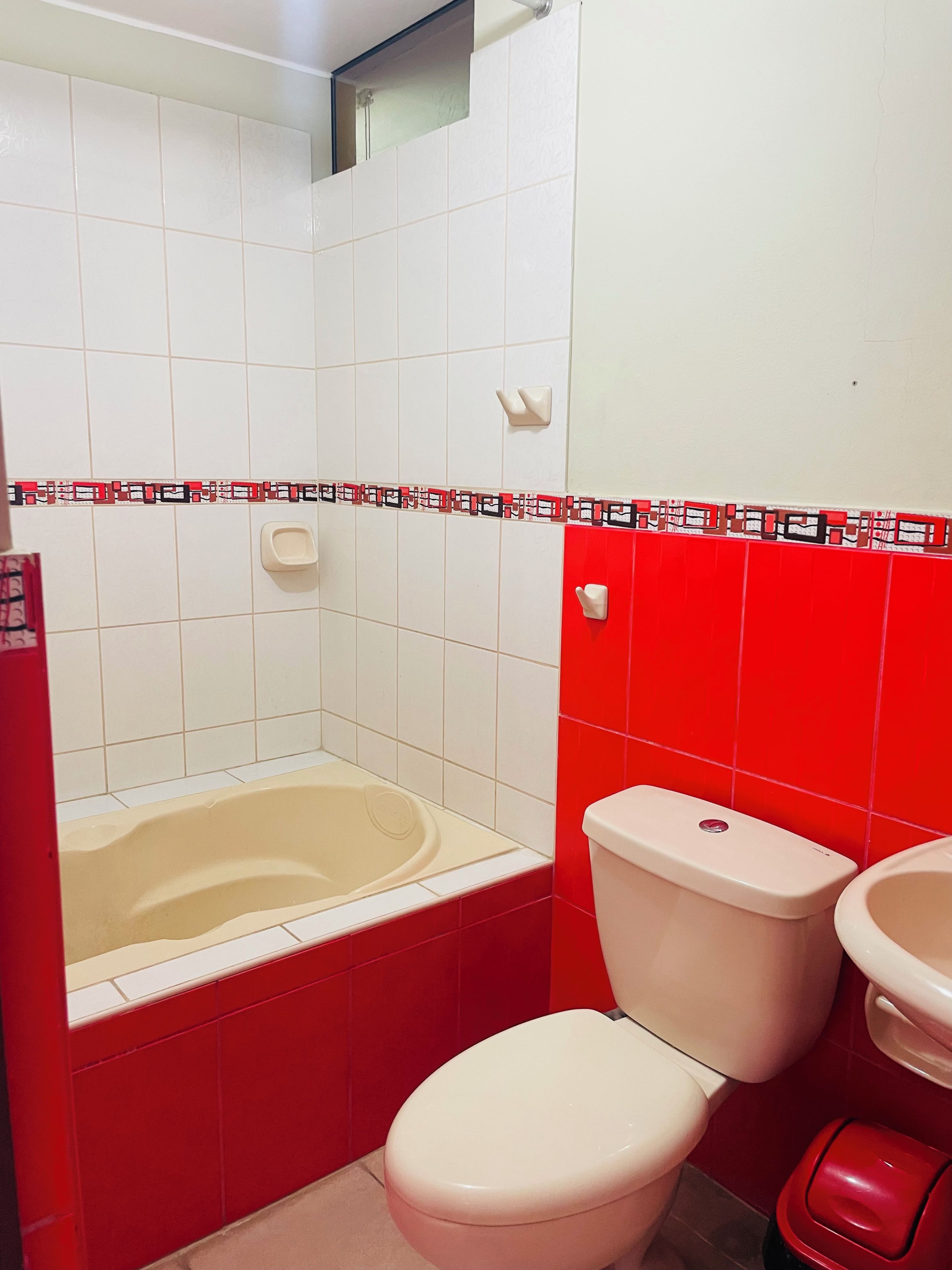 Casa de banho com banheira, sanita e lavatório, com azulejos brancos e vermelhos.