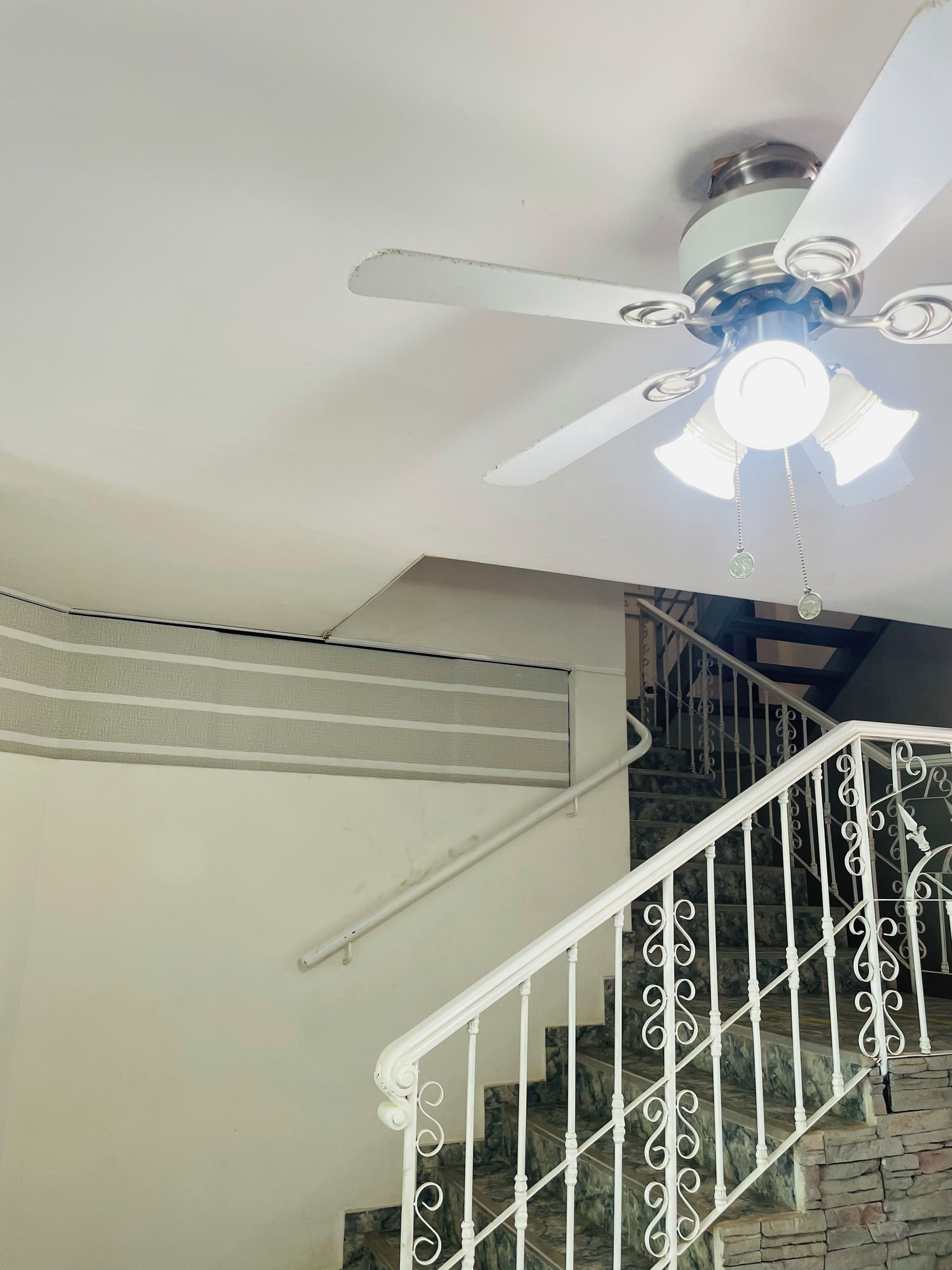 Uma escadaria com corrimãos brancos e um ventilador de teto com luminária.