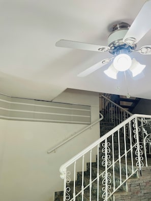 Uma escadaria com corrimãos brancos e um ventilador de teto com luminária.