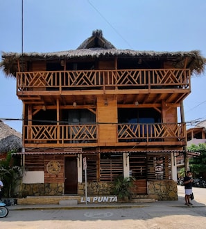 Um edifício de madeira de dois andares com telhado de palha, varanda com guarda-corpos de madeira e uma placa com a inscrição 'LA PUNTA'.
