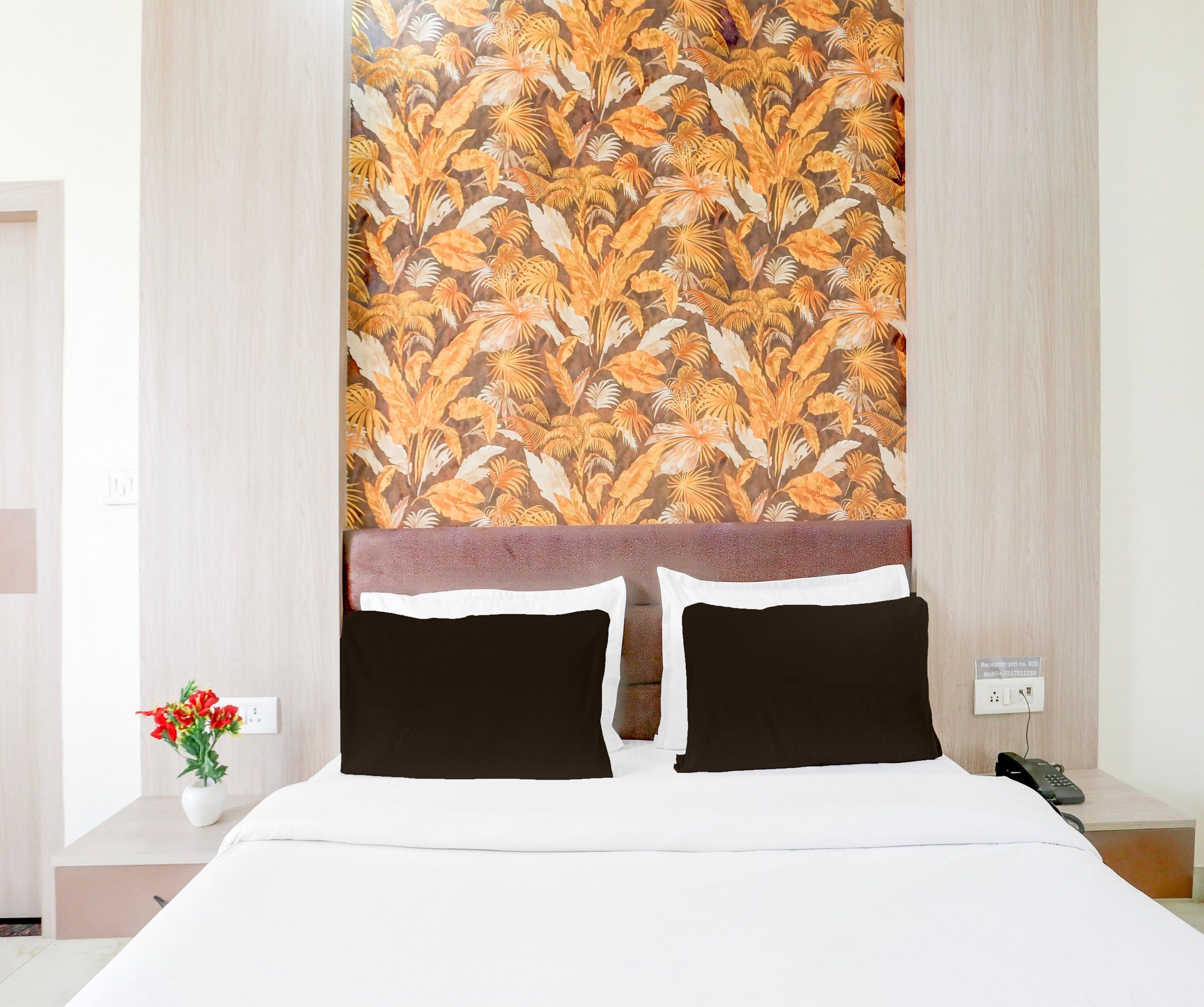 Quarto de hotel com cama, mesa de cabeceira com telefone e parede com desenho de folhagem tropical.