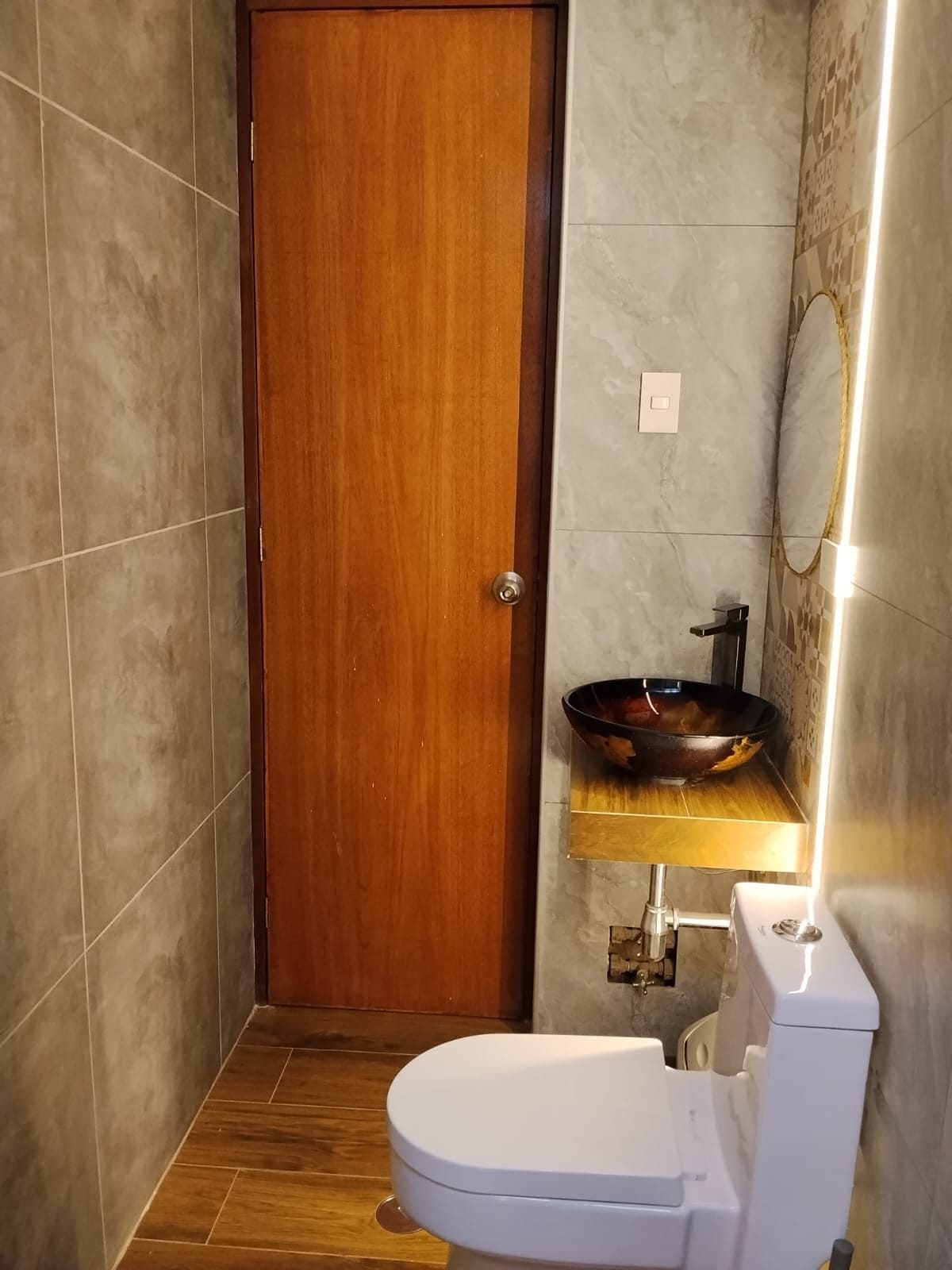 Casa de banho com porta de madeira, sanita branca, lavatório com cuba e espelho.