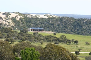 Uma casa com telhado azul numa colina, rodeada por árvores e mais colinas.