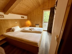 Quarto de cabana de madeira com cama, mesa de cabeceira, janela com cortinas e porta.