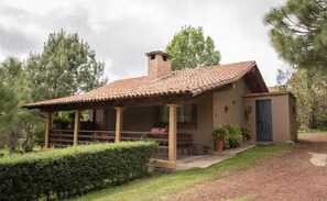 Uma casa térrea com telhado de telhas, varanda coberta e um pequeno jardim.