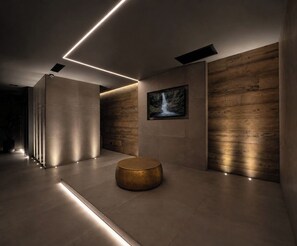 Decoração moderna com mesa redonda dourada, iluminação embutida e pintura de uma cachoeira na parede.