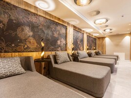 Sala de spa com várias macas de massagem, painéis de madeira e decoração floral nas paredes.