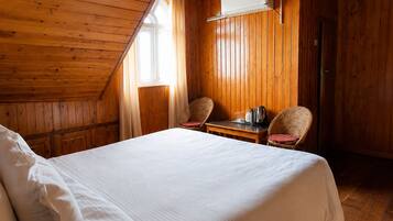 Quarto com cama, duas cadeiras de vime, uma mesinha com chaleira e uma janela.