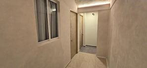 Um corredor estreito com janela, porta e luminária no teto.
