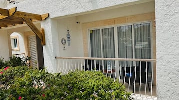 Um edifício branco com varanda, janela com cortinas e um pequeno jardim com arbustos.