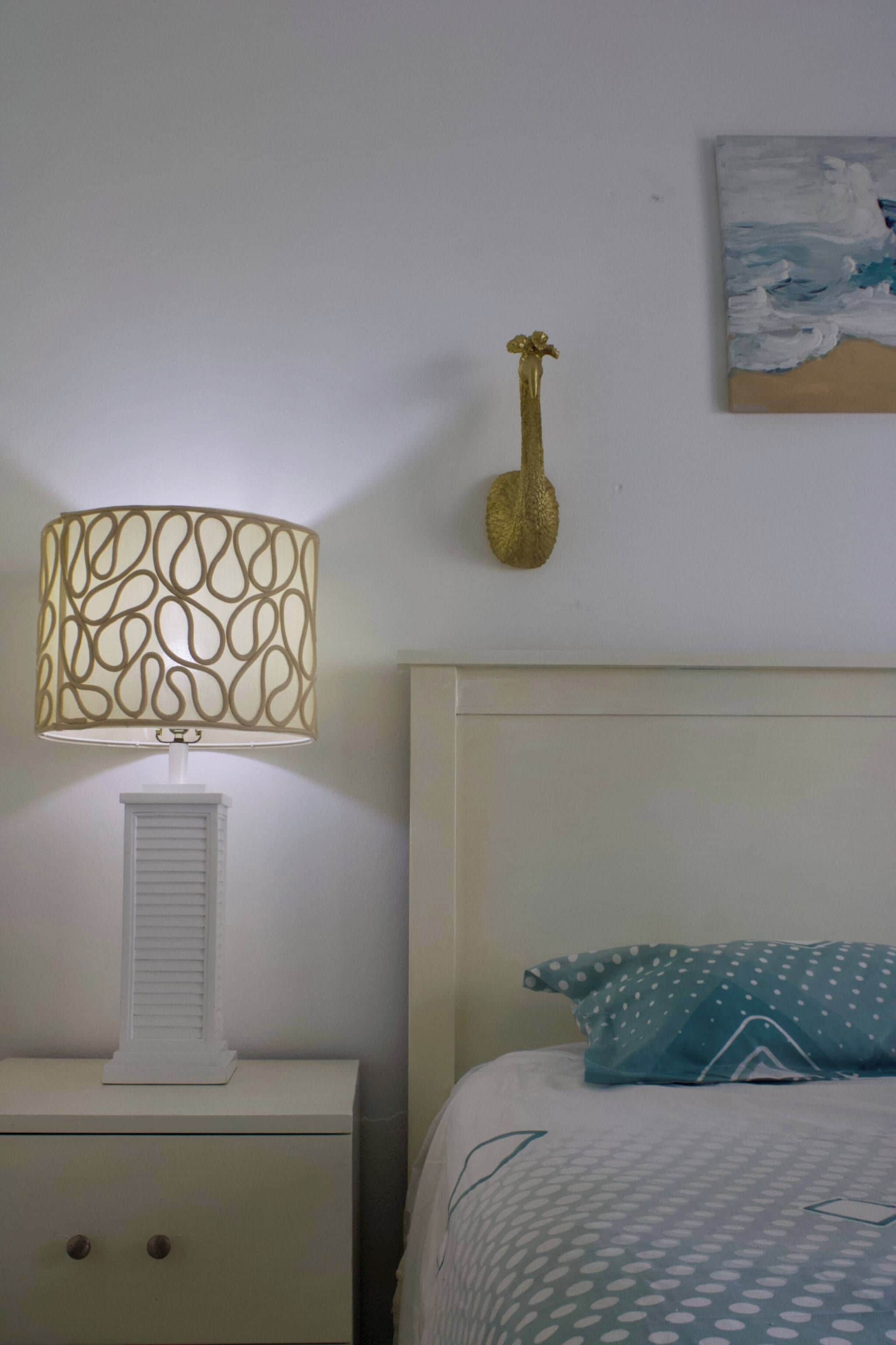 Quarto com luminária de cabeceira, objeto decorativo na parede e cama com roupa de cama estampada.
