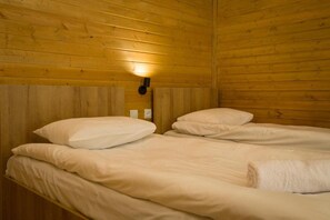 Quarto de cabana de madeira com duas camas, cada uma com roupa de cama e almofadas brancas.