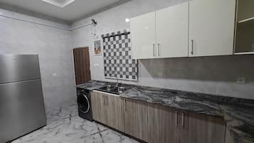 Cozinha moderna com geladeira de aço inoxidável, armários de madeira, máquina de lavar embutida e piso com padrão marmorizado.