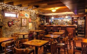 Um bar com mesas e cadeiras de madeira, uma parede de tijolos e um balcão com garrafas.