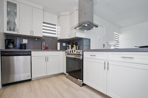 Cozinha moderna com armários brancos, eletrodomésticos de aço inoxidável e bancada cinza.