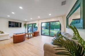 Uma sala de estar espaçosa, com um sofá, uma mesa de centro e uma televisão fixada na parede.