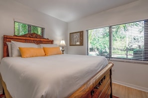 Uma cama bem arrumada com cabeceira de madeira, abajur e janela com persianas.