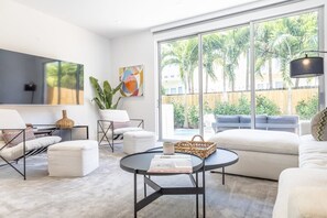 Uma sala de estar moderna com sofá, mesa de centro e uma janela ampla com vista para palmeiras.