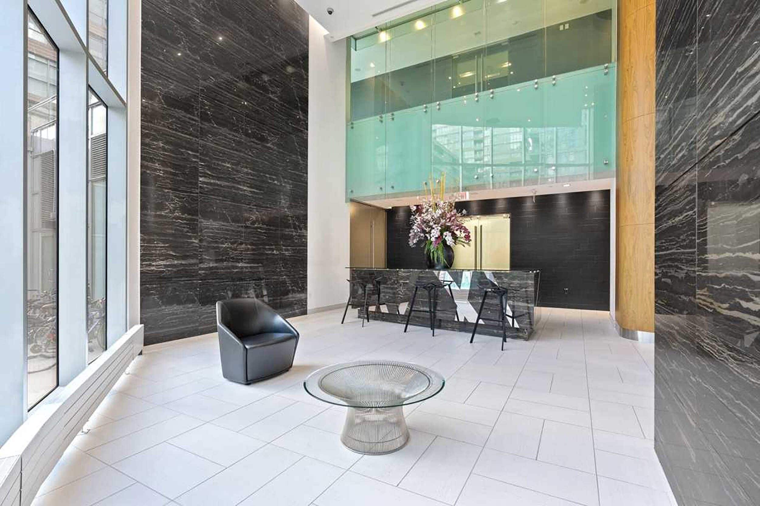 Um lobby moderno com uma mesa de recepção de vidro, uma poltrona de couro preto e uma mesa de centro de vidro.