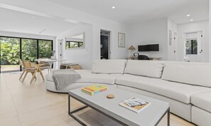 Uma sala de estar moderna com um sofá branco, uma mesa de centro e um espaço de jantar com cadeiras e mesa de madeira.