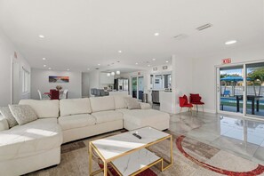 Uma sala de estar moderna com um sofá seccional, uma mesa de centro de mármore e uma cozinha ao fundo.