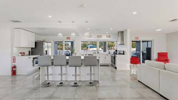 Uma cozinha moderna com armários brancos, uma ilha central com banquetas e um sinal de saída.