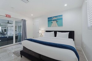 Quarto de hotel com uma cama, um quadro de um cais, sinal de saída e uma porta de vidro deslizante para uma varanda.