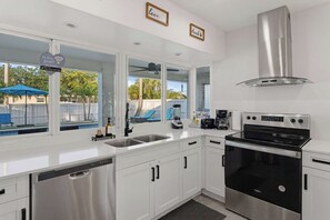 Cozinha moderna com eletrodomésticos de aço inoxidável, forno embutido e uma grande janela com vista para a área da piscina.