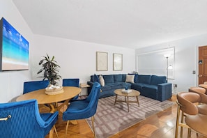 Uma sala de estar moderna com um sofá azul, uma mesa de centro de madeira e uma mesa de jantar com cadeiras.