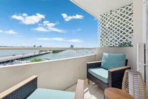 Uma varanda com vista para um rio, uma cadeira, uma mesa pequena e uma parede com padrão.