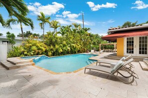 Piscina com deck ladrilhado, espreguiçadeiras e palmeiras.
