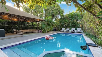 Piscina com um flutuador, rodeada por espreguiçadeiras e um espaço coberto para sentar.