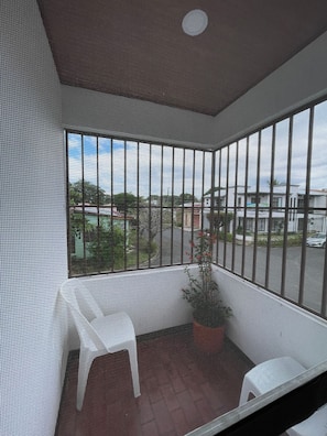 Quarto com uma janela grande, uma cadeira branca e um vaso de planta.