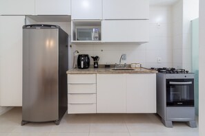 Uma cozinha compacta com geladeira de aço inoxidável, micro-ondas, fogão a gás e cafeteira.