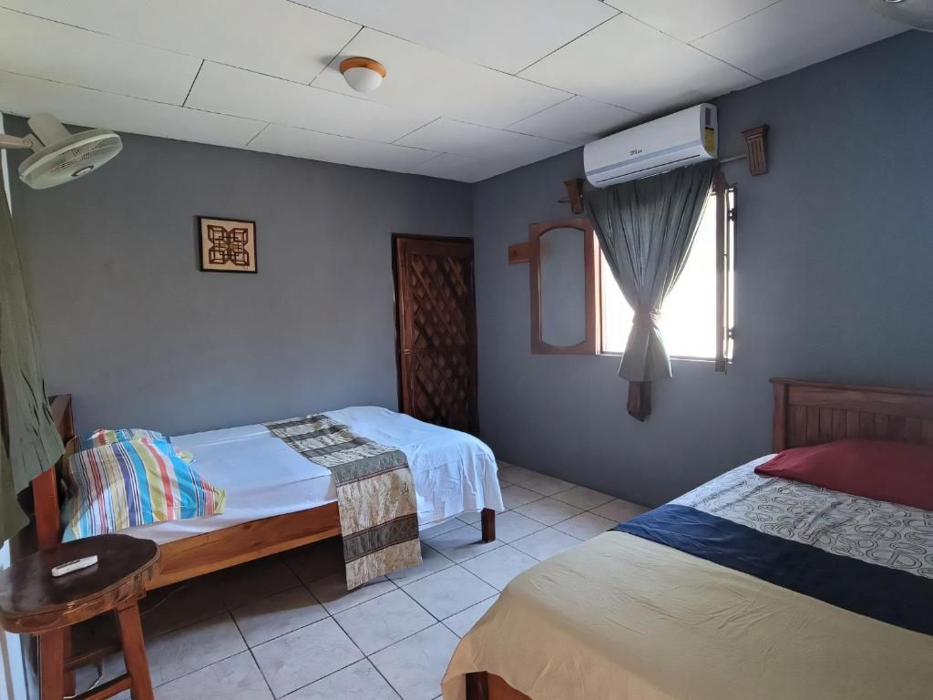 Quarto com duas camas, ventoinha no teto, ar condicionado e janela com cortinas.