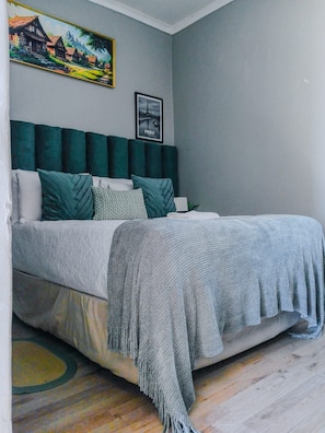 Quarto com cama, cabeceira, almofadas, cobertor, quadro emoldurado e pintura na parede.