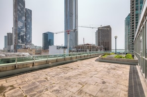 Terraço no telhado com vista para edifícios altos, uma guindaste de construção e um corpo de água.