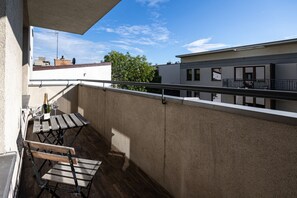 Varanda com mesa e cadeiras de madeira, uma garrafa de vinho e vista para prédios e árvores vizinhos.