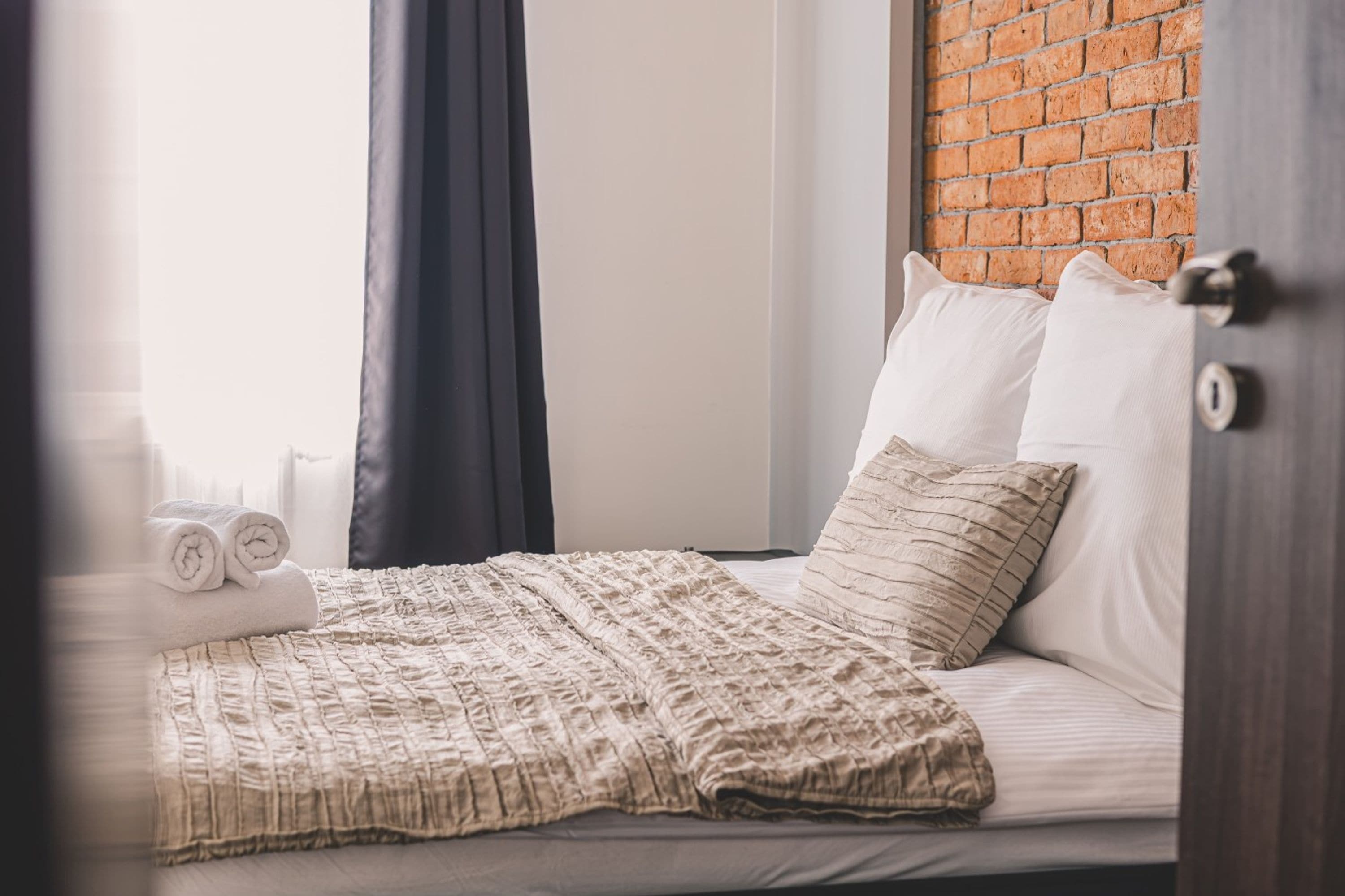 Cama bem arrumada com manta texturizada, travesseiros brancos e toalhas dobradas sobre um colchão branco.