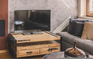 Uma sala de estar moderna com uma televisão de tela plana sobre um móvel de madeira, um sofá com almofadas e uma mesinha com um vaso.