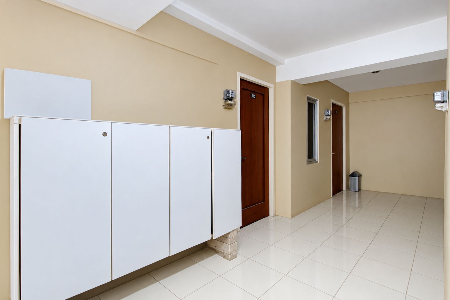 Um corredor com armários brancos, uma porta de madeira e uma lixeira.