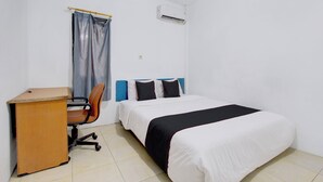 Quarto com cama, escrivaninha, cadeira, janela com cortinas e aparelho de ar condicionado.