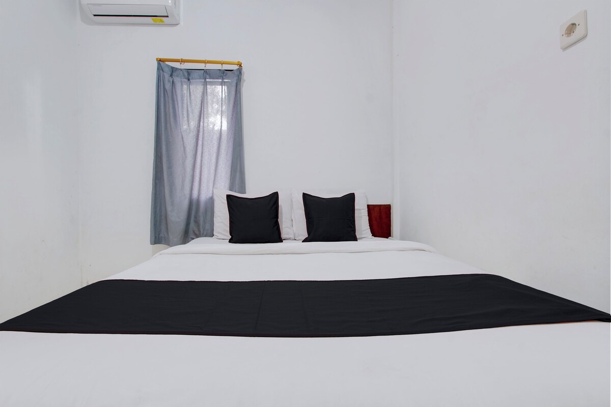 Uma cama com edredom preto e branco, duas almofadas pretas e uma almofada vermelha.