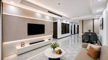 Uma sala de estar moderna com televisão de tela plana, uma mesa de centro com frutas, um sofá e um espaço de jantar com cadeiras.