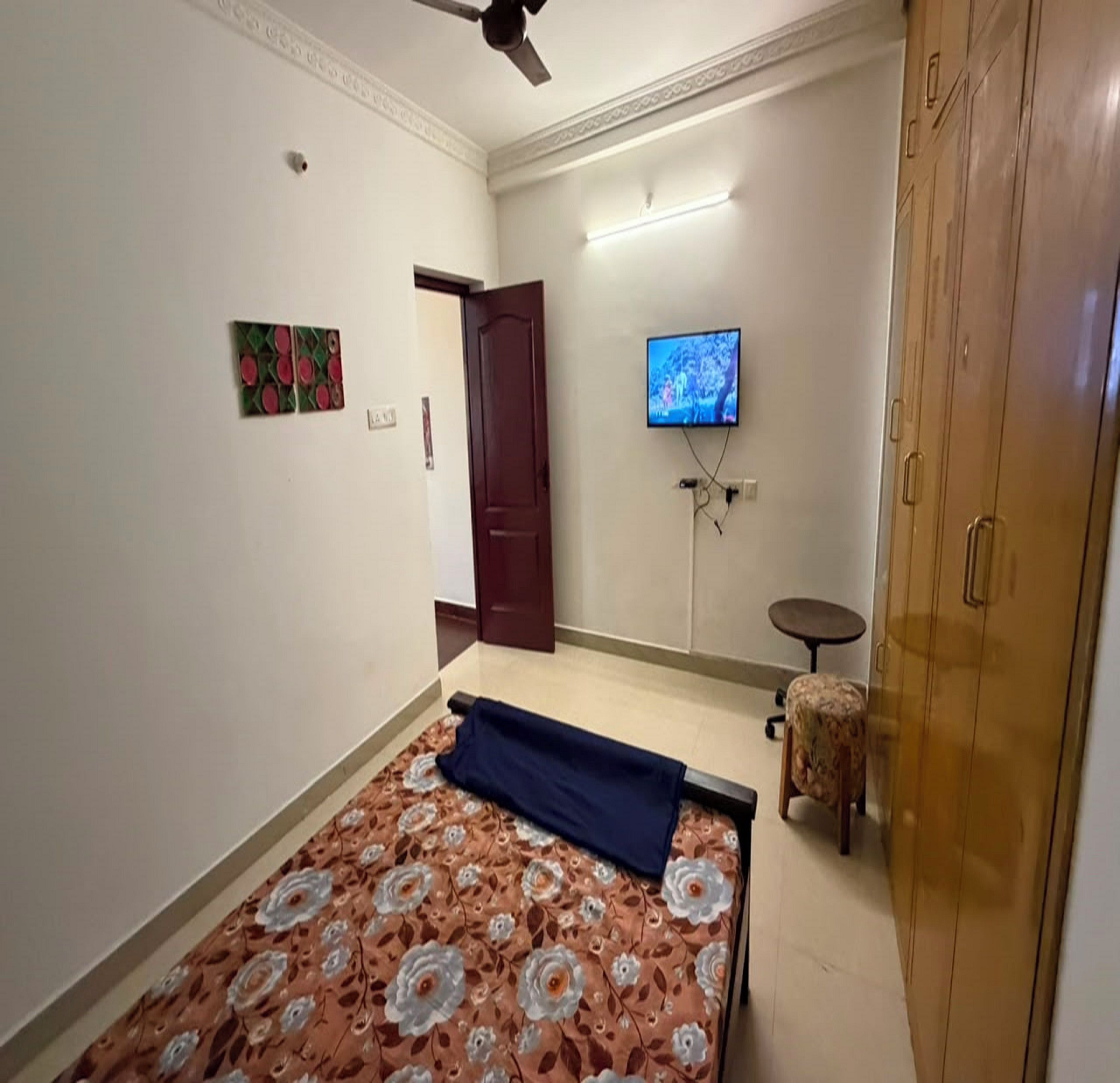 Quarto com cama, televisão na parede, guarda-roupa e uma pequena mesa.